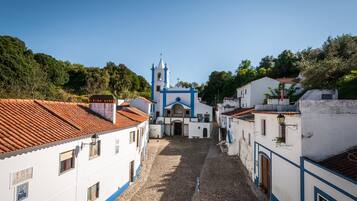 Uma rua de calçada estreita ladeada por edifícios com fachadas azuis e brancas, conduzindo a uma igreja com um campanário.