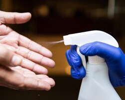 Uma pessoa vestindo luvas azuis usando um frasco spray branco.