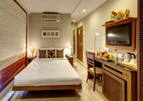 Quarto de hotel com cama, escrivaninha com televisão, cadeira, cesta de frutas e ar condicionado fixado na parede.