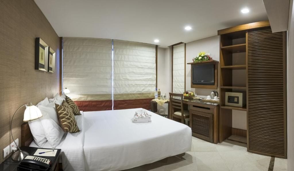 Quarto de hotel com uma cama grande, uma escrivaninha com cadeira, televisão e um minibar.
