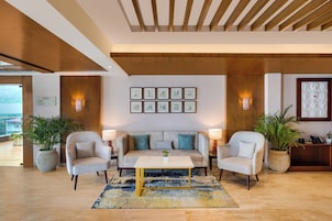 Um lobby moderno com um sofá, duas poltronas, uma mesa de centro e plantas em vasos.