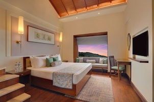 Quarto com cama, mesa de cabeceira, cadeira e televisão.