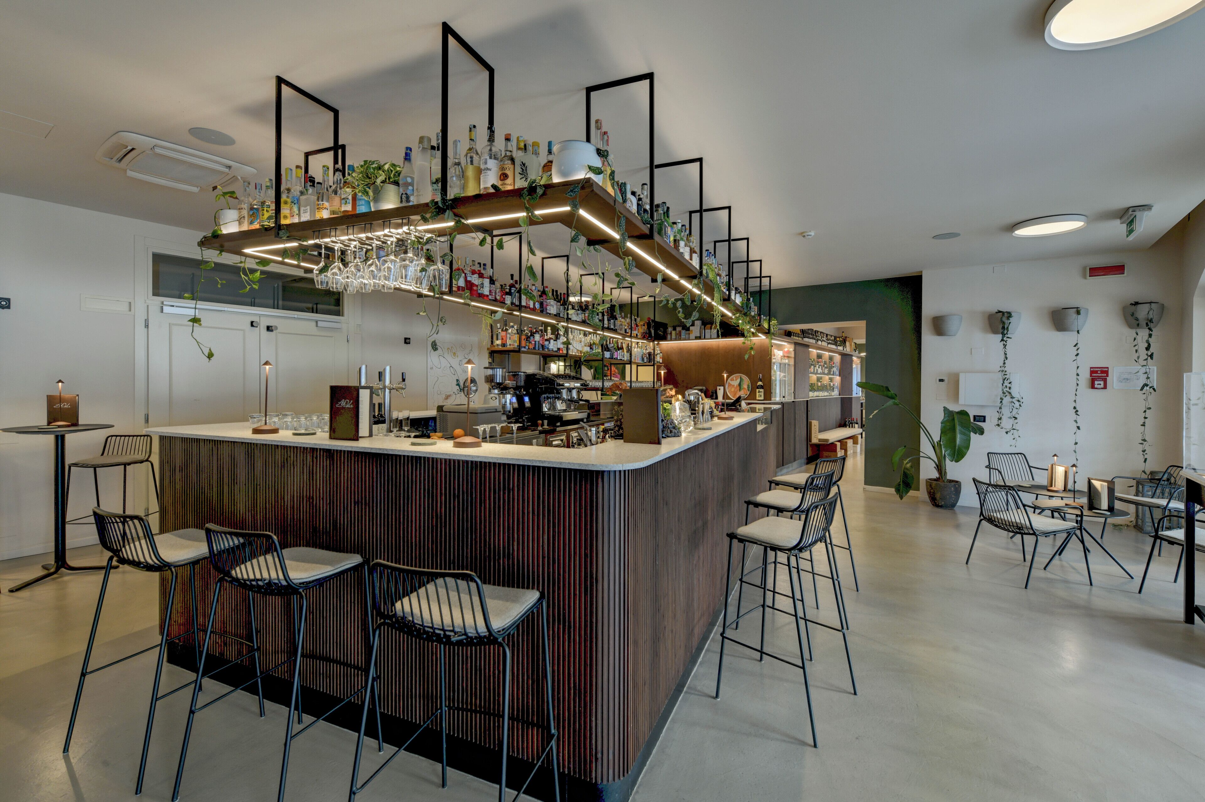 Uma área de bar moderna, com balcão de madeira, diversas opções de assento e variedade de garrafas e copos.
