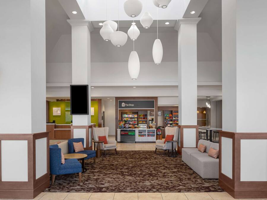 Um saguão de hotel com áreas de estar, uma loja e luminárias pendentes.