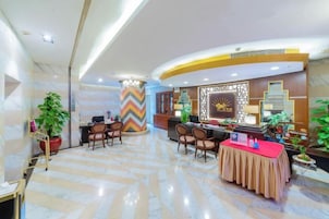 Um hall de hotel com balcão de recepção, área de estar e plantas decorativas.