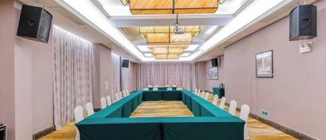 Sala de conferências com uma mesa comprida, cadeiras e luminária no teto.