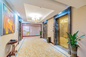Um corredor de hotel com carpete estampado, um lustre e uma pintura grande na parede.