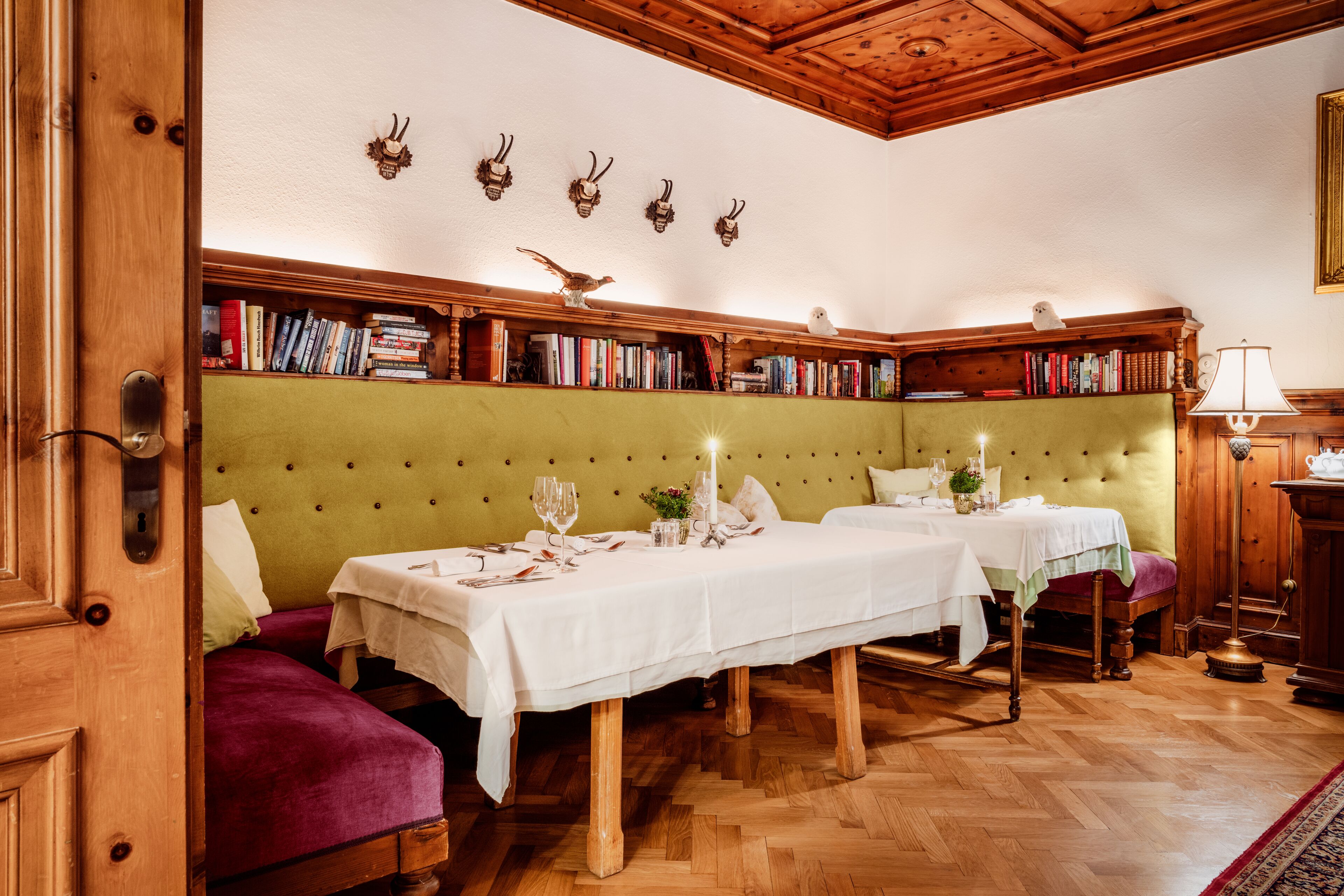 Uma sala de jantar com uma mesa comprida posta para dois, uma cabeceira estofada verde e estantes cheias de livros.