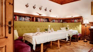 Uma sala de jantar com uma mesa comprida posta para dois, uma cabeceira estofada verde e estantes cheias de livros.