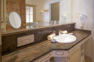 Casa de banho com bancada de granito, lavatório branco, espelho e porta-toalhas.