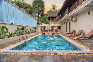 Piscina com espreguiçadeiras e guarda-sóis, cercada por plantas e um muro de madeira.