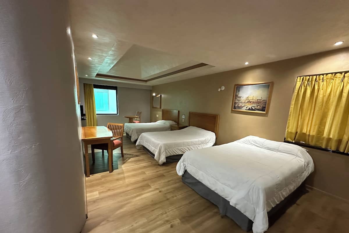 Quarto de hotel com duas camas de solteiro, uma escrivaninha de madeira, uma cadeira e uma mesinha.