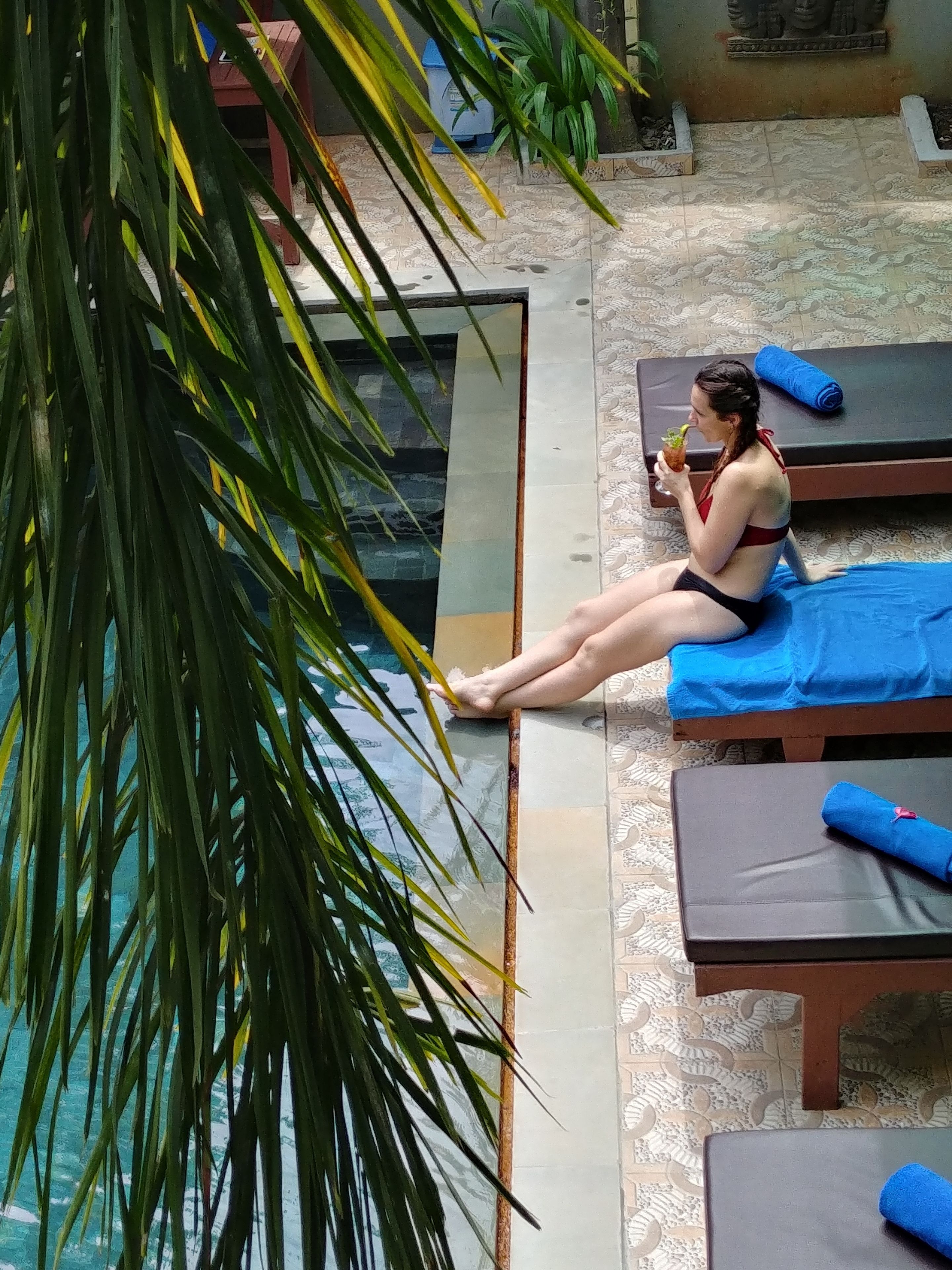 Uma pessoa sentada em uma espreguiçadeira azul perto de uma piscina, segurando uma bebida.
