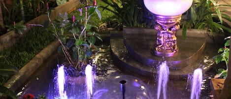 Uma fonte com vários jatos de água e um vaso decorativo em um jardim.