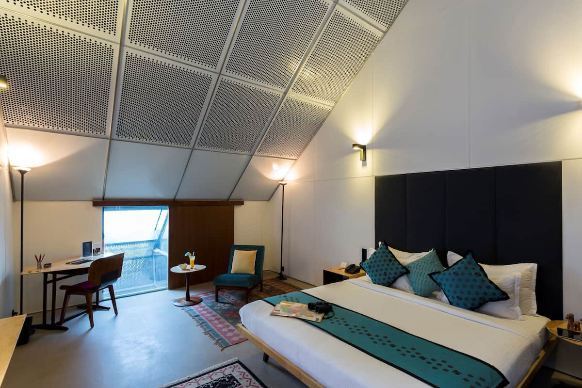 Quarto de hotel moderno com uma cama grande, uma escrivaninha, uma cadeira e uma mesinha.