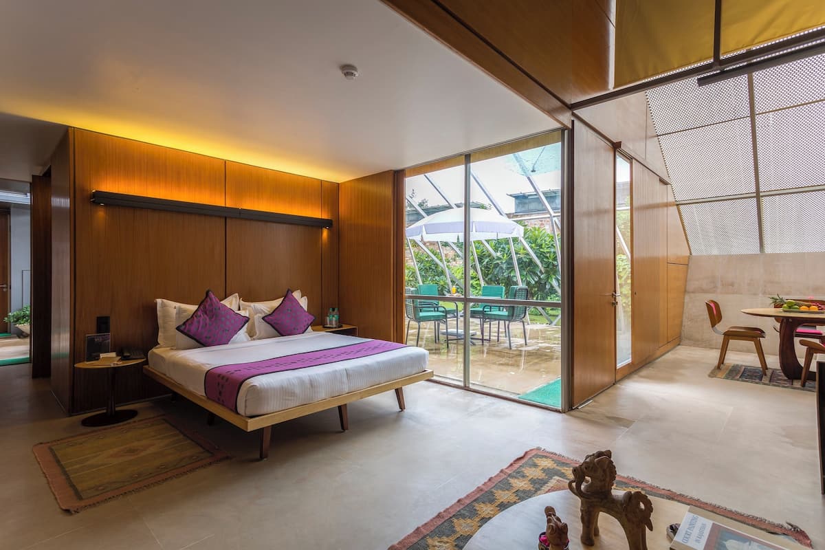 Quarto moderno com uma cama grande, uma mesinha e vista para o exterior através de uma porta de correr de vidro.