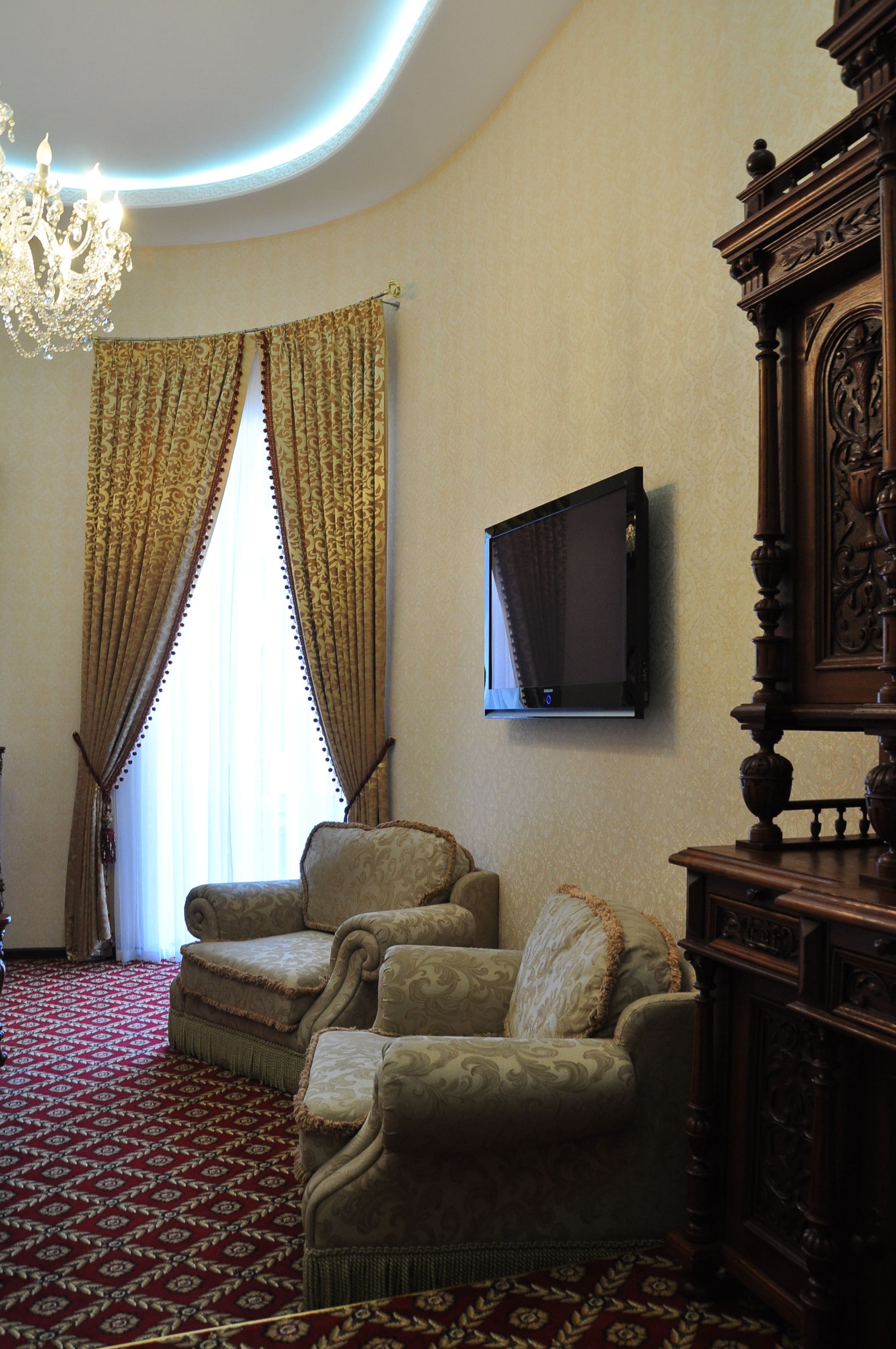 Quarto com lustre, televisão na parede e duas poltronas.