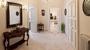 Um corredor com chão de mármore, um console de madeira com objetos decorativos, um espelho redondo, um relógio e um radiador.
