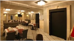 Um hall de hotel com várias mesas de jantar, cadeiras e uma grande porta preta.