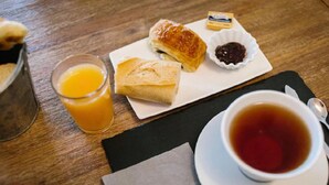 Uma mesa de madeira com uma travessa de pastelaria, um copo de sumo de laranja e uma chávena de chá.