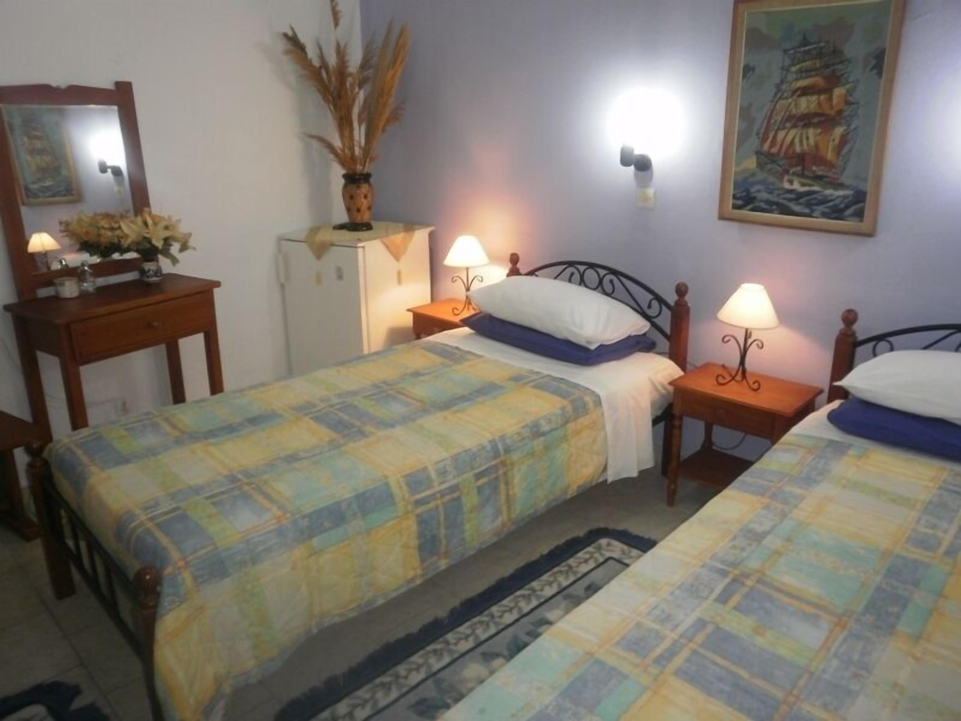 Quarto com duas camas, cômoda, espelho, abajur e um quadro na parede.
