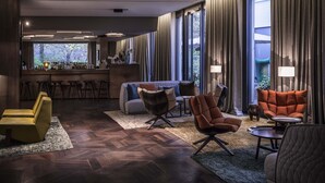 Um lobby moderno de hotel com área de bar, espaços para sentar e grandes janelas que proporcionam luz natural.