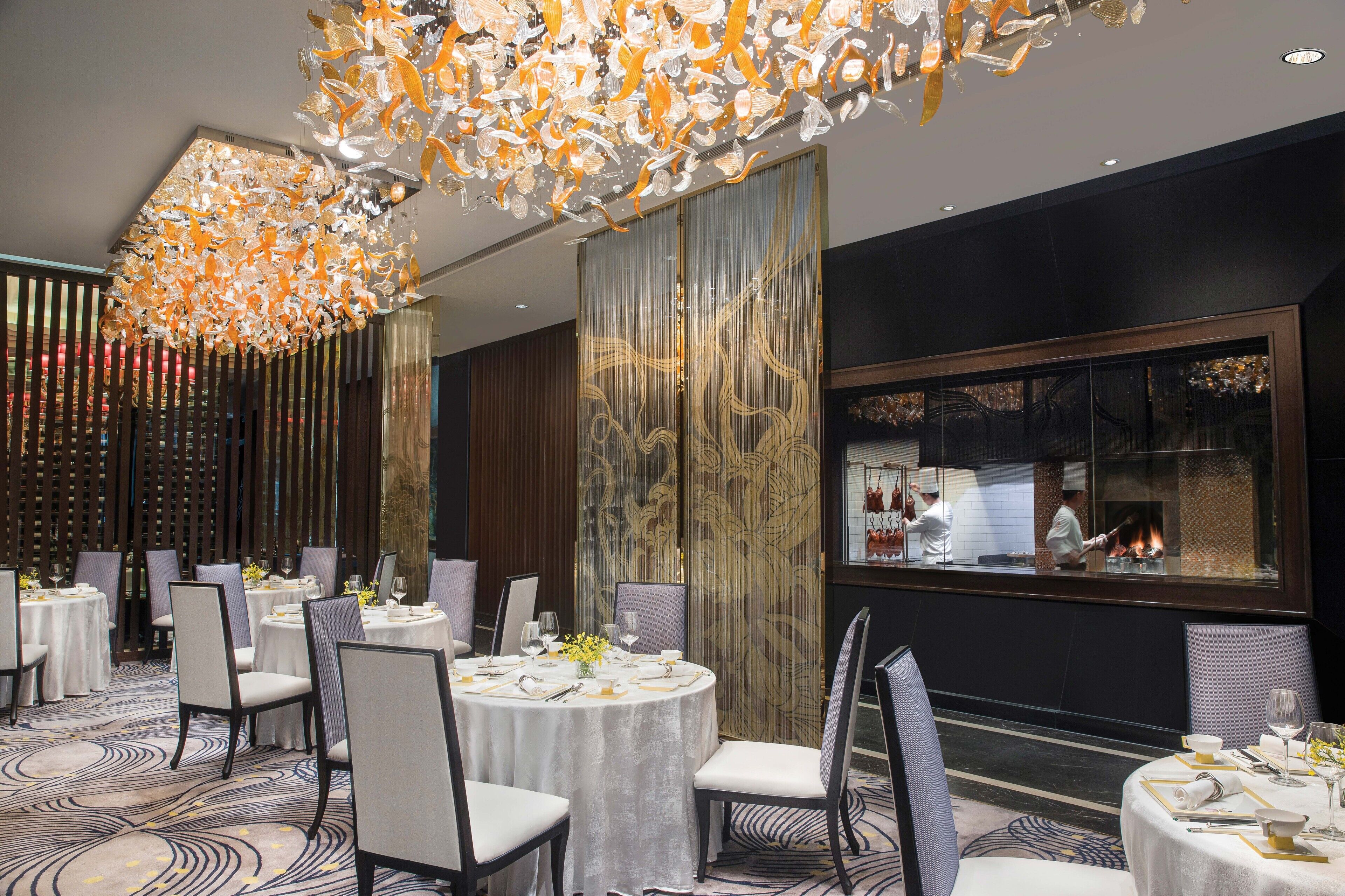 Um restaurante com mesas redondas, cadeiras e um teto decorativo.
