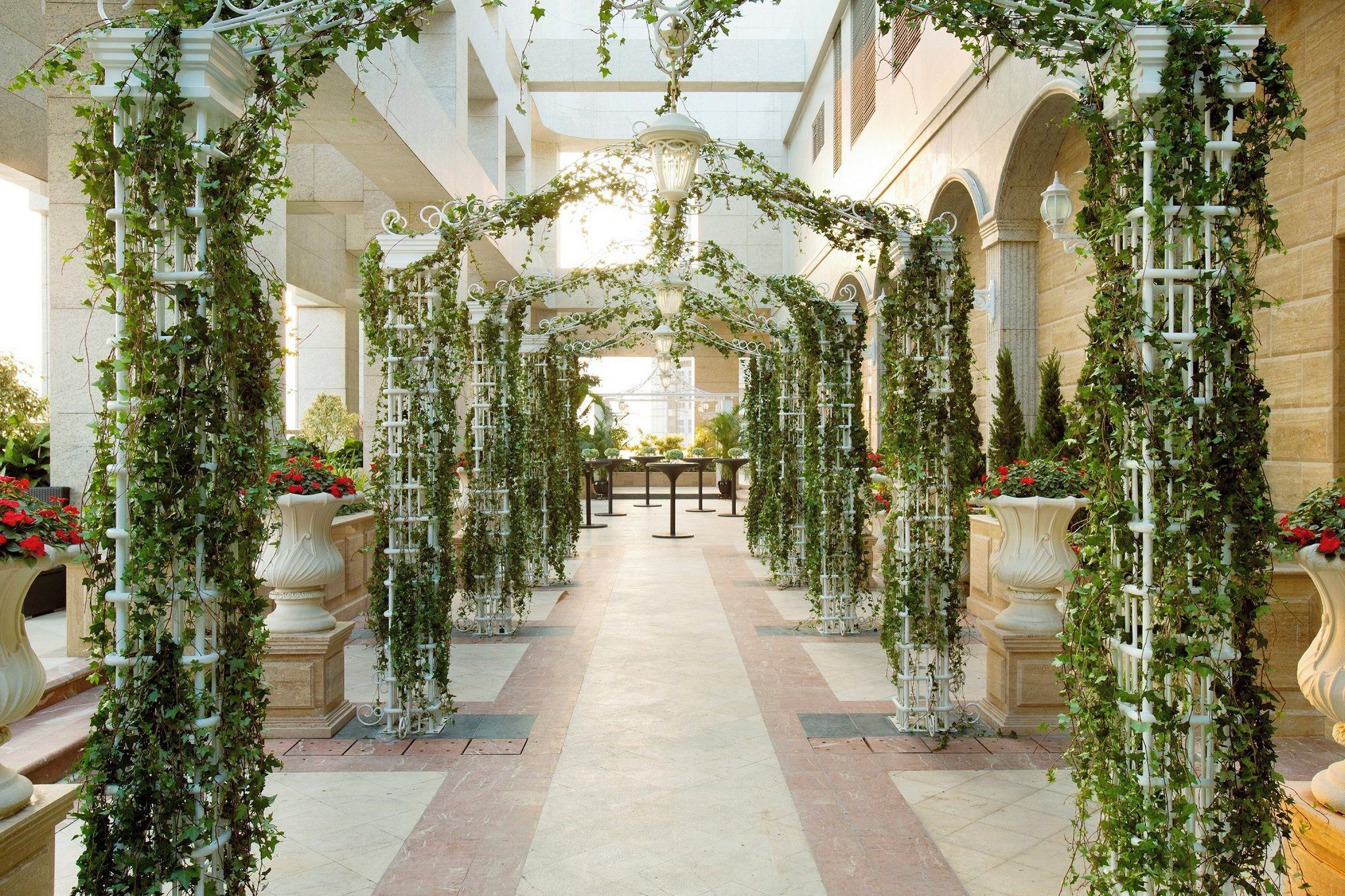 Corredor interno com arcos e colunas, decorado com plantas e folhagem.