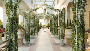 Corredor interno com arcos e colunas, decorado com plantas e folhagem.