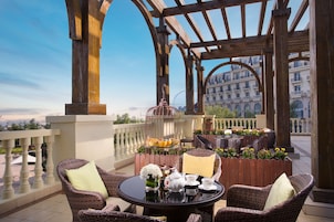 Um terraço com mobiliário de vime, uma mesa com chávena e chá, e uma gaiola de pássaros com flores.