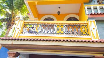Um edifício amarelo com varanda, uma palmeira e telhado telhado.