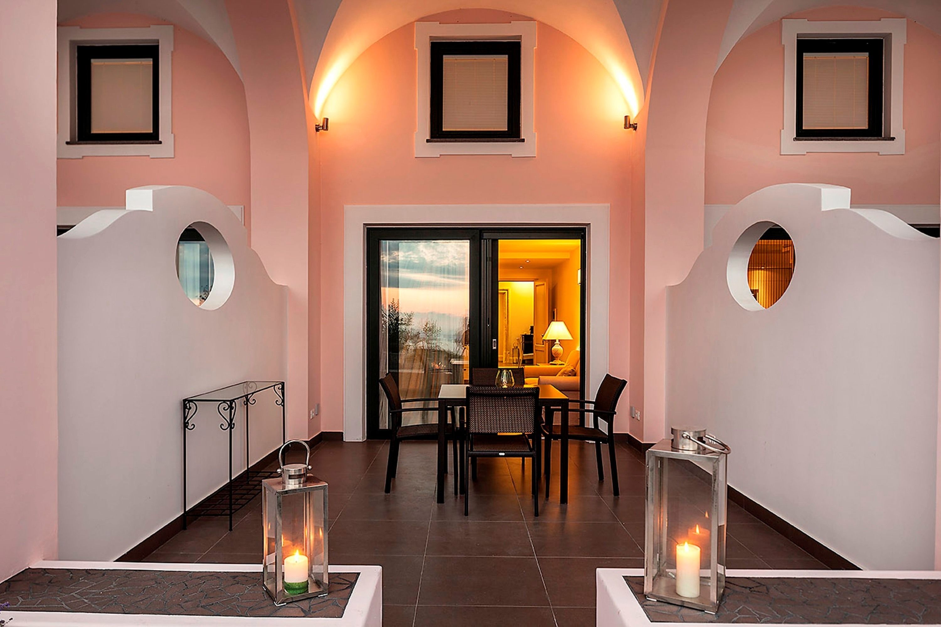 Um interior moderno com área de refeições, duas velas acesas e vista através de uma porta de vidro.