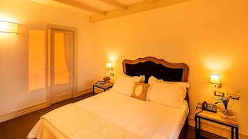 Uma cama bem arrumada com cabeceira de madeira, duas mesas de cabeceira com luminárias e uma porta com cortina.