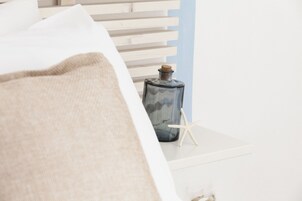 Um sofá branco com almofada texturizada, um frasco azul escuro com rolha e uma estrela-do-mar decorativa sobre uma superfície branca.