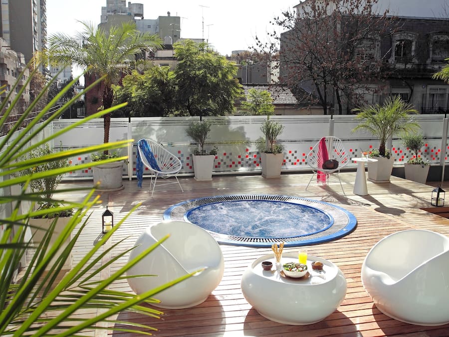 Área de piscina no terraço com hidromassagem, espreguiçadeiras e plantas em vasos.