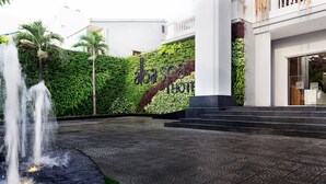 Entrada de hotel com um espelho de água, uma parede verde com plantas trepadoras e uma escadaria que leva à entrada.