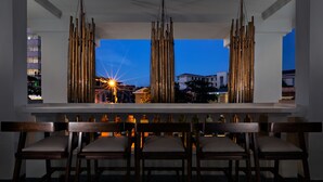 Zona de bar com cadeiras de madeira e vista para a cidade ao entardecer.