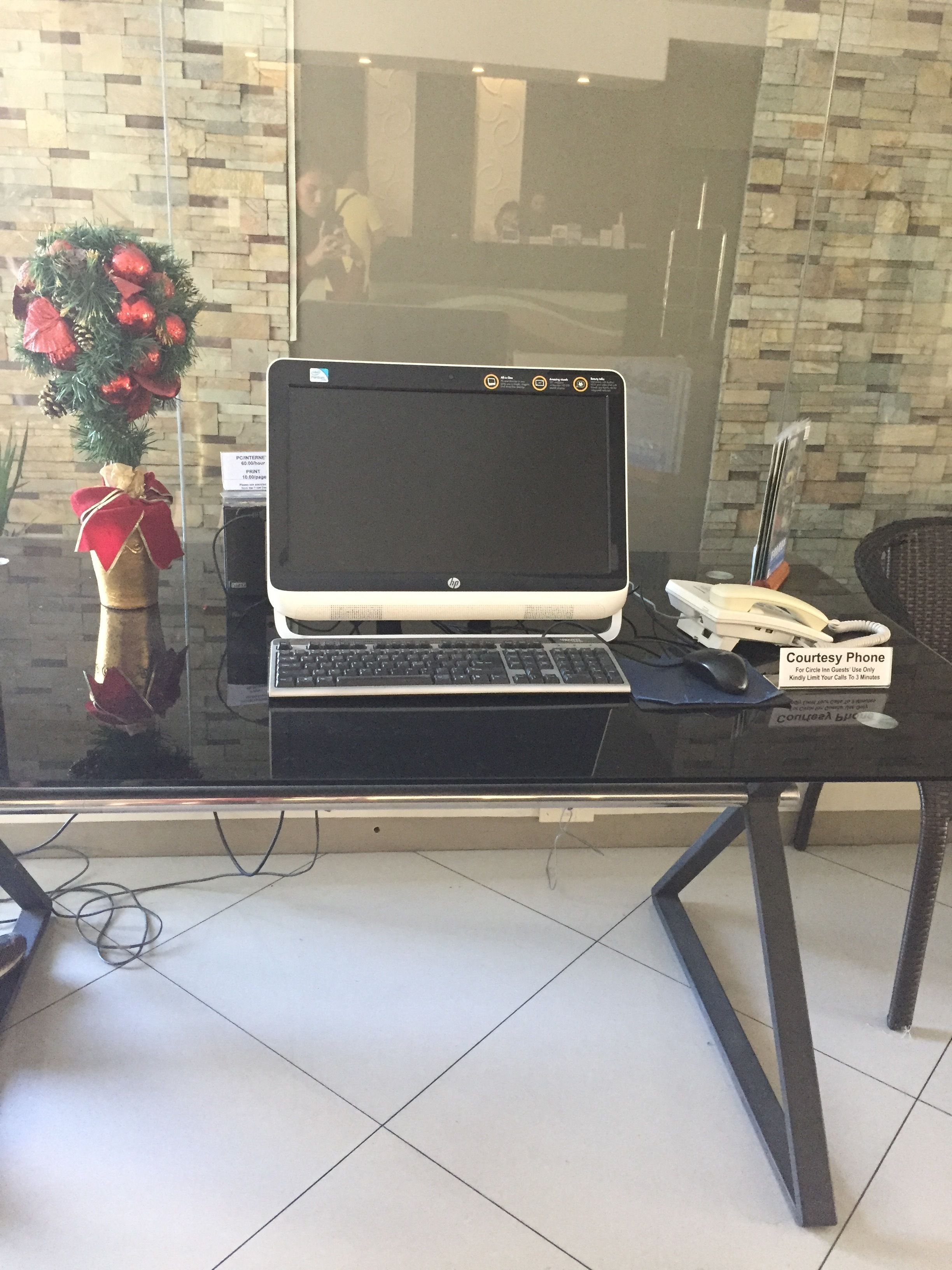 Um laptop sobre uma mesa de vidro, com um telefone e uma placa indicando uso do telefone cortesia.