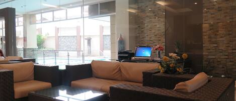 Um lobby moderno com divisória de vidro, assentos confortáveis, um laptop sobre uma mesa e um vaso decorativo com flores.