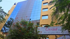 Edifício de hotel com fachada de vidro moderna, um letreiro indicando que é o 'Hotel Orritel', e um aviso dizendo 'Seu Anfitrião Completo'.