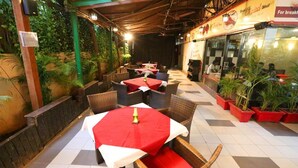 Restaurante ao ar livre com mesas e cadeiras, cercado por vegetação e área coberta.