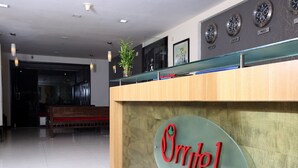 Uma receção com uma placa a indicar "Ortel West" e relógios a mostrar as horas de Londres, Paris e Nova Iorque.