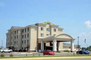 Um hotel Holiday Inn Express com entrada central, vários andares e um estacionamento com diversos veículos.
