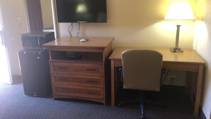 Quarto de hotel com escrivaninha de madeira, televisão, luminária, cadeira, micro-ondas e geladeira.