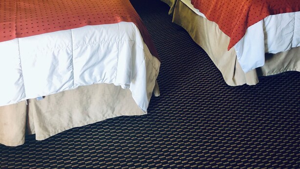 Quarto de hotel com duas camas, uma mesa de cabeceira com abajur e uma obra de arte emoldurada na parede.
