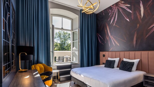 Quarto de hotel moderno com uma cama grande, uma escrivaninha, uma cadeira e vista para o exterior.