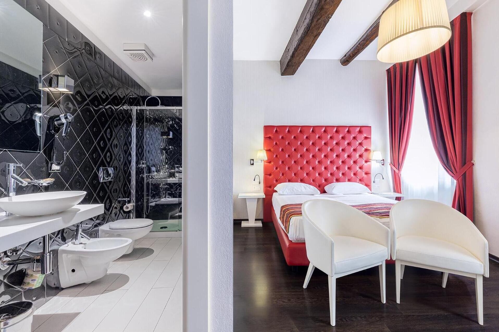 Quarto de hotel moderno com cabeceira vermelha, cadeiras brancas e uma grande janela com cortinas vermelhas.