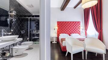 Quarto de hotel moderno com cabeceira vermelha, cadeiras brancas e uma grande janela com cortinas vermelhas.