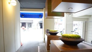 Uma área de recepção moderna com um balcão de madeira, um grande vaso com plantas e um toldo azul ao fundo.