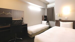 Quarto de hotel com duas camas de solteiro, uma secretária com cadeira, televisão, guarda-roupa e telefone.